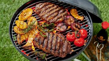 Uma churrasqueira com bife, batatas, cebolas e tomates.