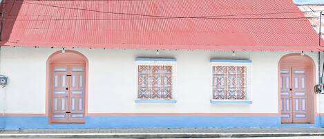 Um edifício com telhado vermelho, duas portas cor-de-rosa e duas janelas com grades decorativas.