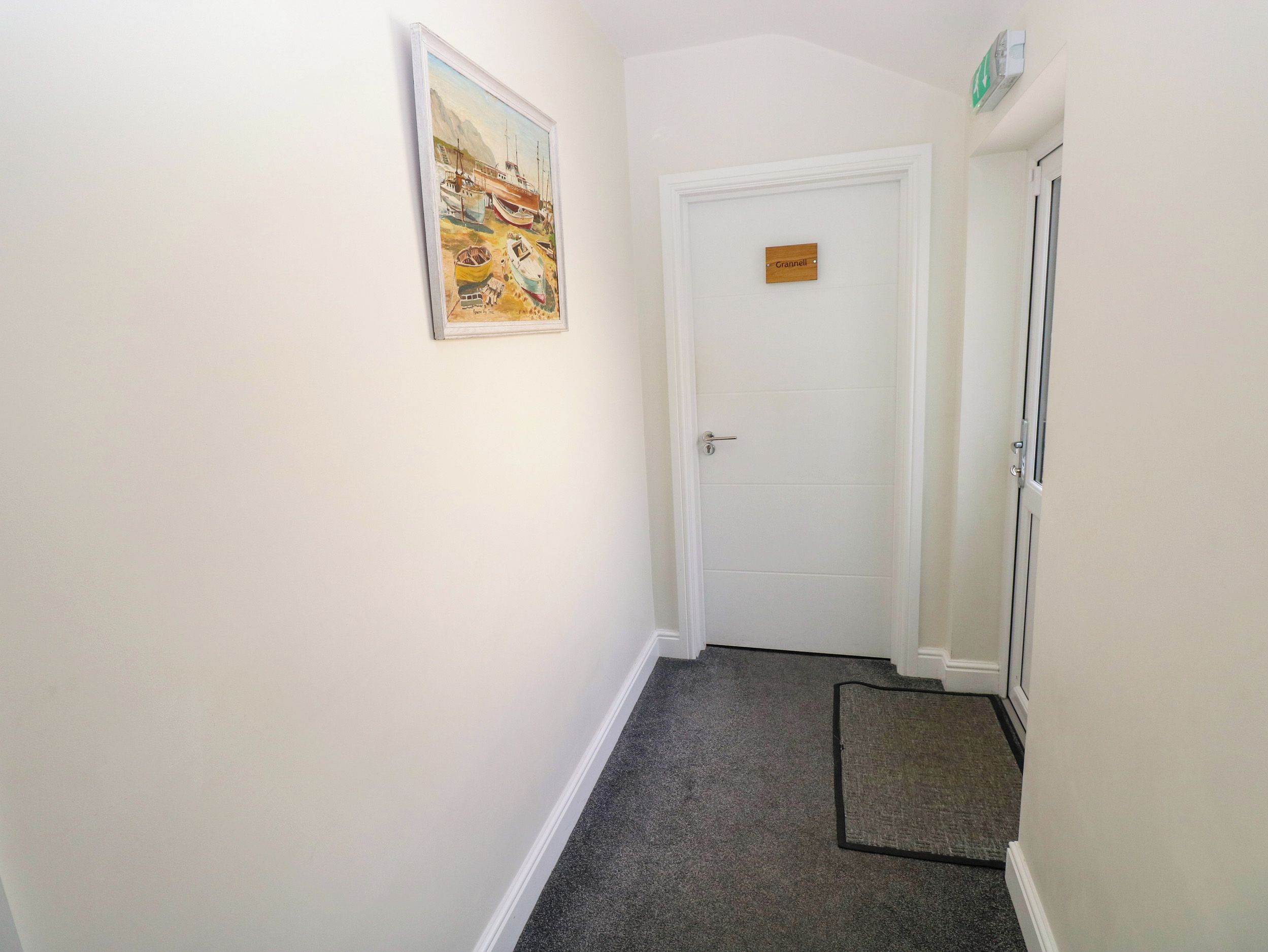 Um corredor com porta, tapete de entrada e um quadro na parede.