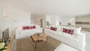 Uma sala de estar moderna com dois sofás brancos, uma mesa de centro de madeira e uma televisão de tela plana.