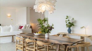 Uma área de refeições com mesa e cadeiras de madeira, um vaso branco com flores e uma luminária pendente moderna.