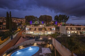 Um hotel moderno com piscina no terraço, área de estar ao ar livre e vista para o horizonte da cidade.