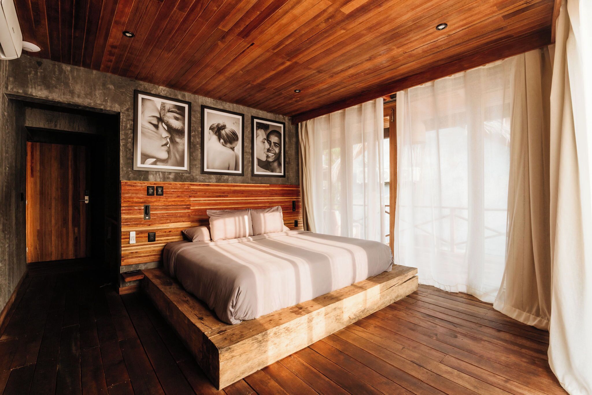 Quarto com teto de madeira, cama com estrutura de madeira e três quadros na parede.
