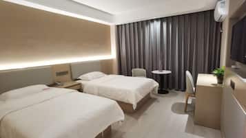 Quarto de hotel com duas camas, uma escrivaninha, uma cadeira, uma mesinha, uma televisão e uma cortina.