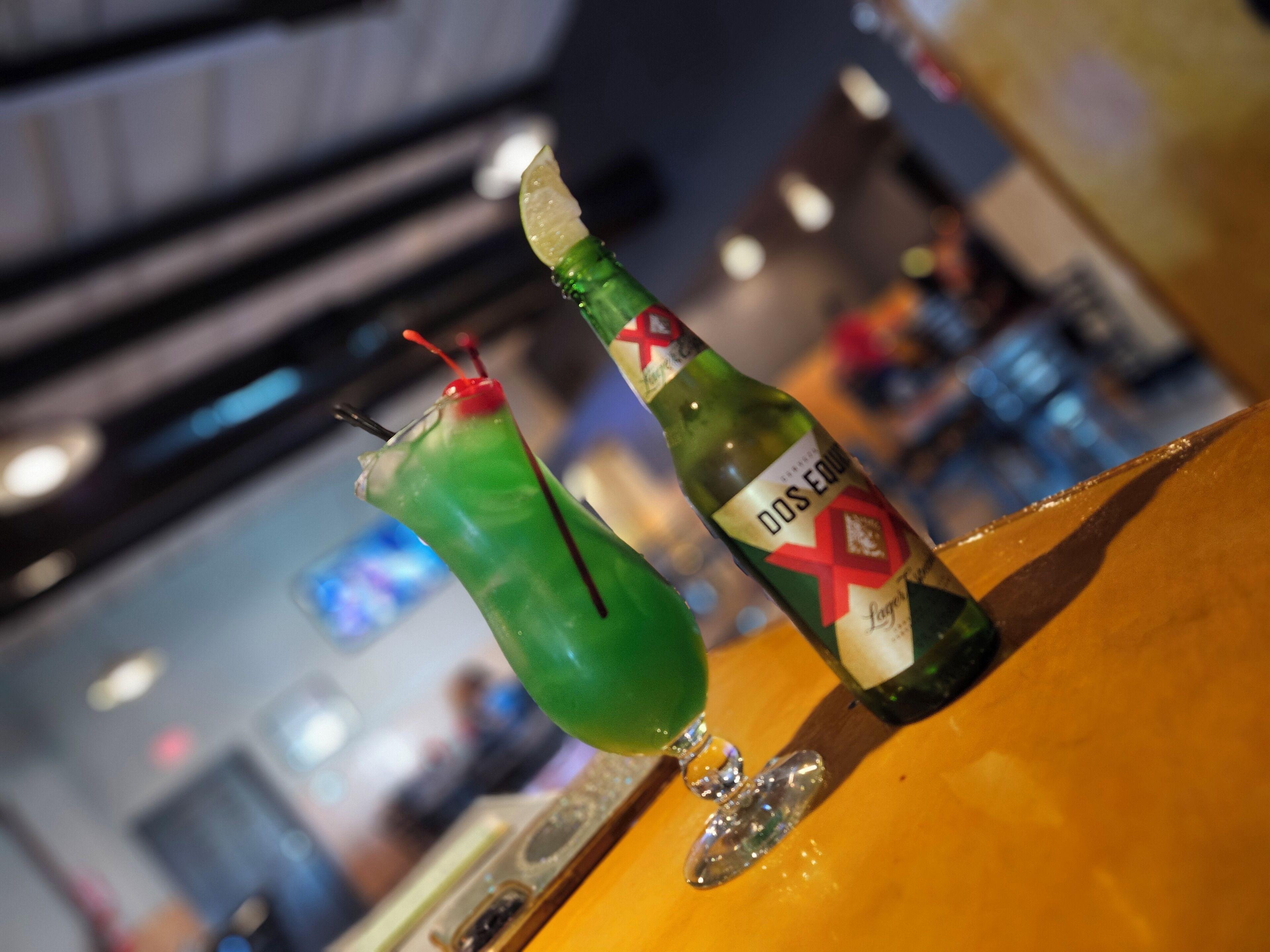 Um bar com um cocktail verde e uma garrafa com o rótulo "DOS EDOU" sobre uma superfície de madeira.
