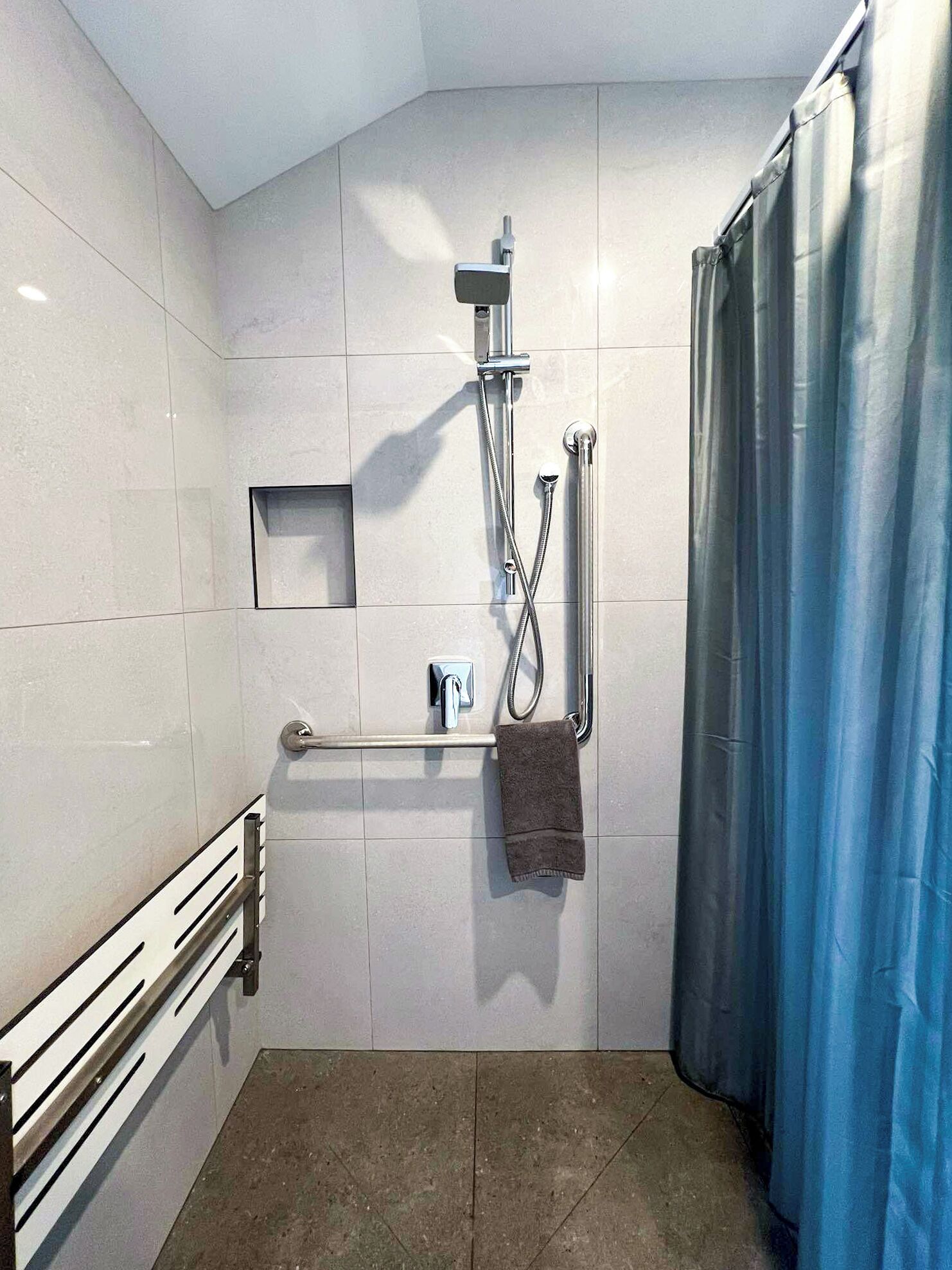 Casa de banho moderna com chuveiro, barra de apoio e porta-toalhas.