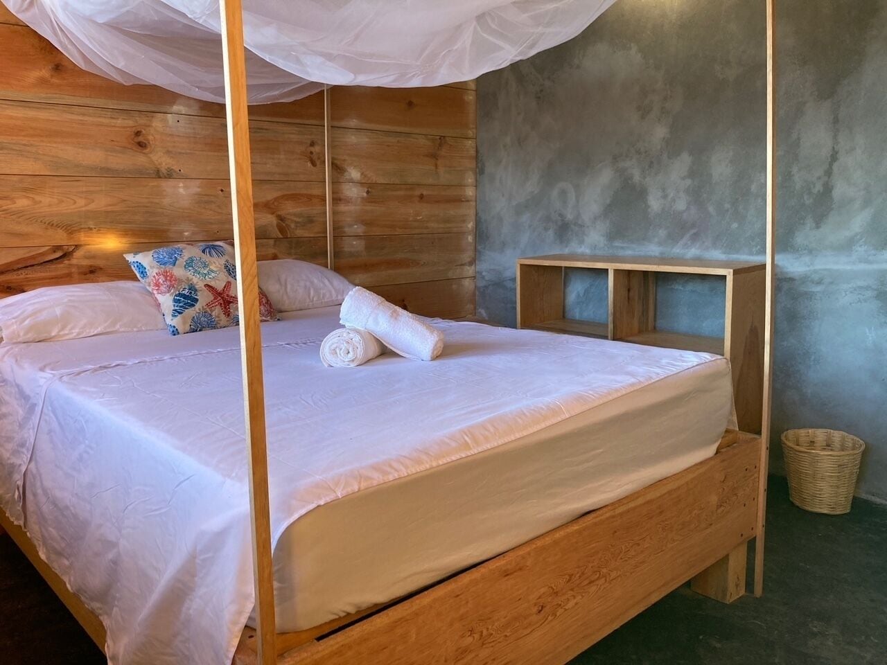 Uma cama de madeira com dossel, roupa de cama branca e almofada decorativa.