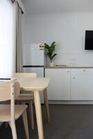 Cozinha compacta com geladeira branca, um pequeno vaso com planta e uma mesa de madeira com cadeiras.