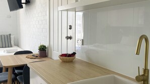 Uma cozinha moderna com azulejos brancos tipo metrô, bancada de madeira, pia embutida com torneira dourada e uma TV de tela plana na parede.