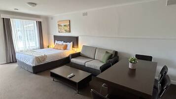 Quarto de hotel moderno com cama, sofá, mesa de jantar e cadeiras.