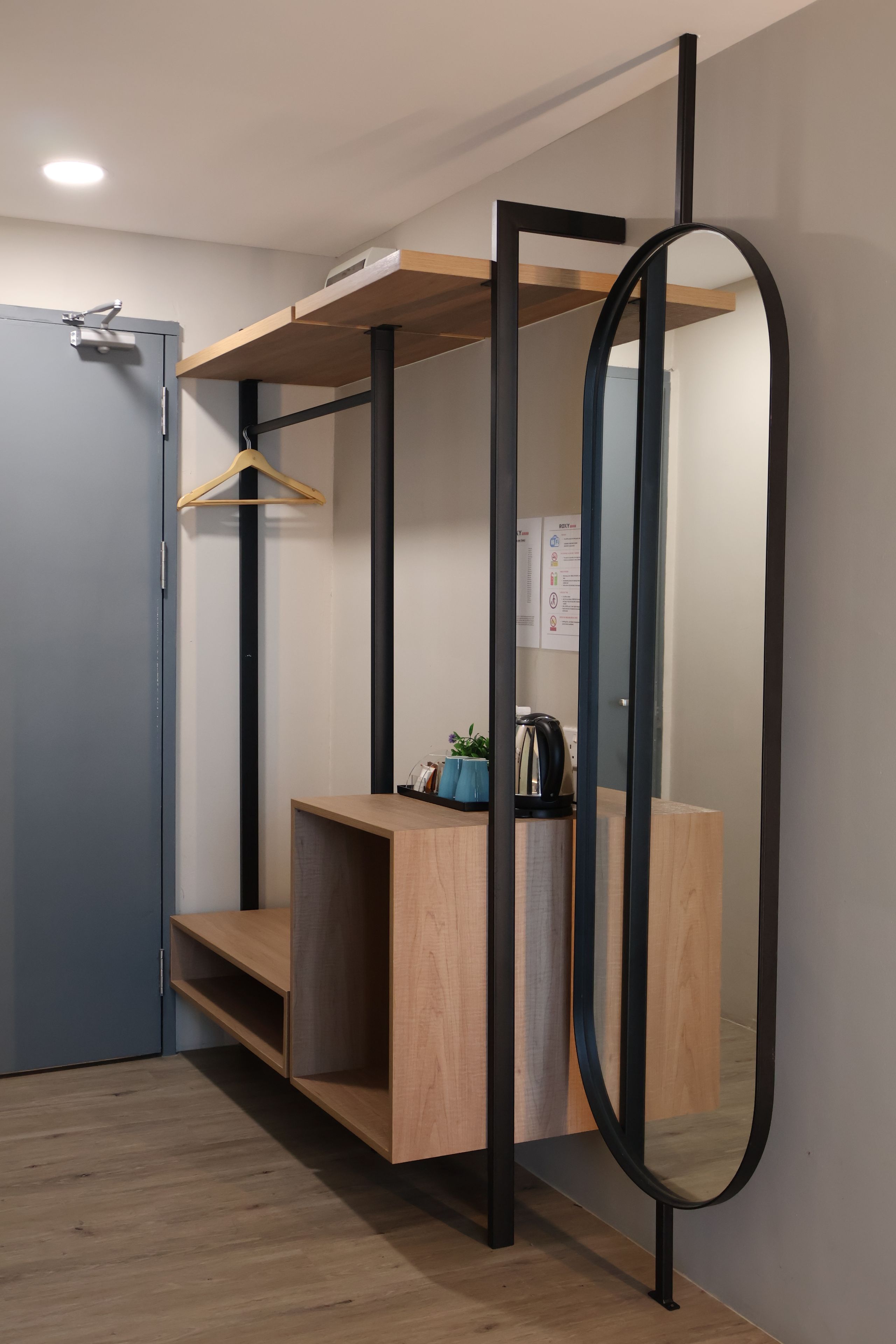 Quarto compacto com escrivaninha, cabideiro, espelho e porta.