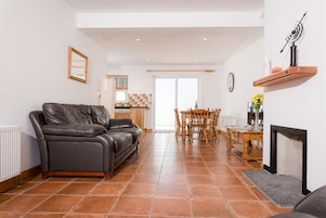Sala de estar com sofá de couro, mesa de jantar com cadeiras, lareira e cozinha ao fundo.