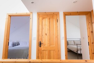 Um quarto com porta de madeira, uma cama com estrutura metálica e uma pequena mesa.