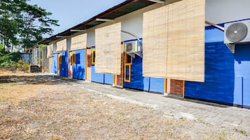 Uma fileira de edifícios azuis com janelas e portas grandes, alguns com toldos de bambu, e um aparelho de ar condicionado à direita.