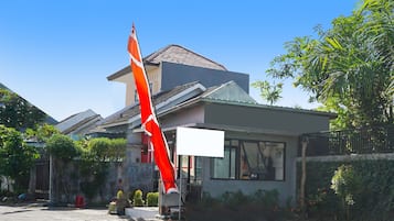 Um edifício moderno com uma bandeira vermelha em destaque, uma grande janela e uma área de entrada pavimentada.