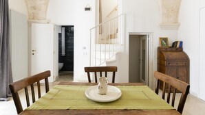 Uma área de refeições com uma mesa posta para dois, um jarro sobre um prato e uma escadaria que leva a um andar superior.