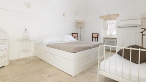 Quarto branco com cama, mesas de cabeceira, abajur e radiador.