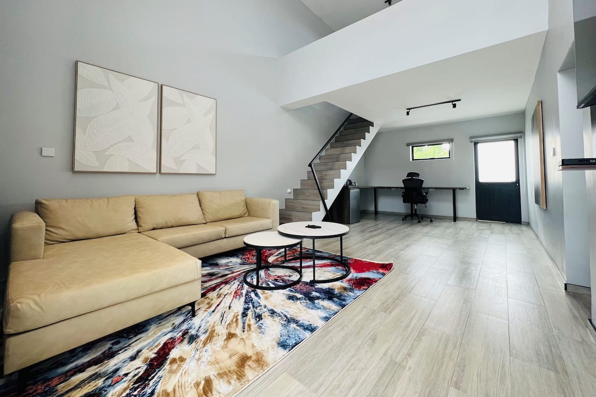 Uma sala de estar moderna com um sofá bege, uma mesa de centro e arte abstrata na parede.