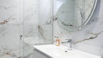Um banheiro moderno com chuveiro em box de vidro, toucador de mármore branco e um espelho grande.