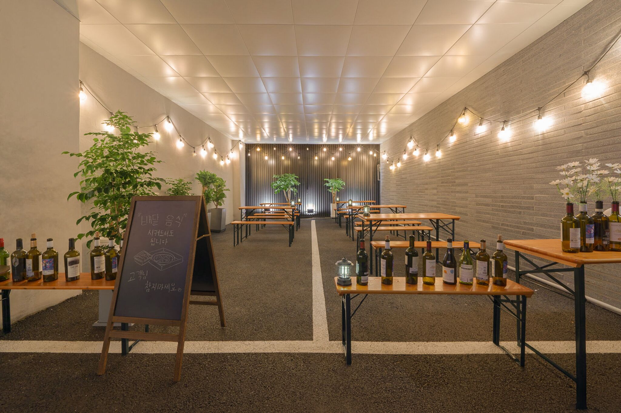 Um espaço interior moderno com mesas, bancos, plantas em vasos e garrafas de vinho.