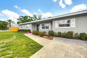 Uma casa térrea com fachada cinza, persianas brancas e porta verde.