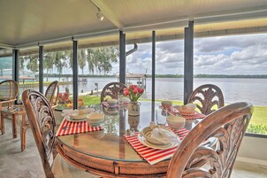 Uma sala de jantar com mesa de vidro, cadeiras e vista para um lago.