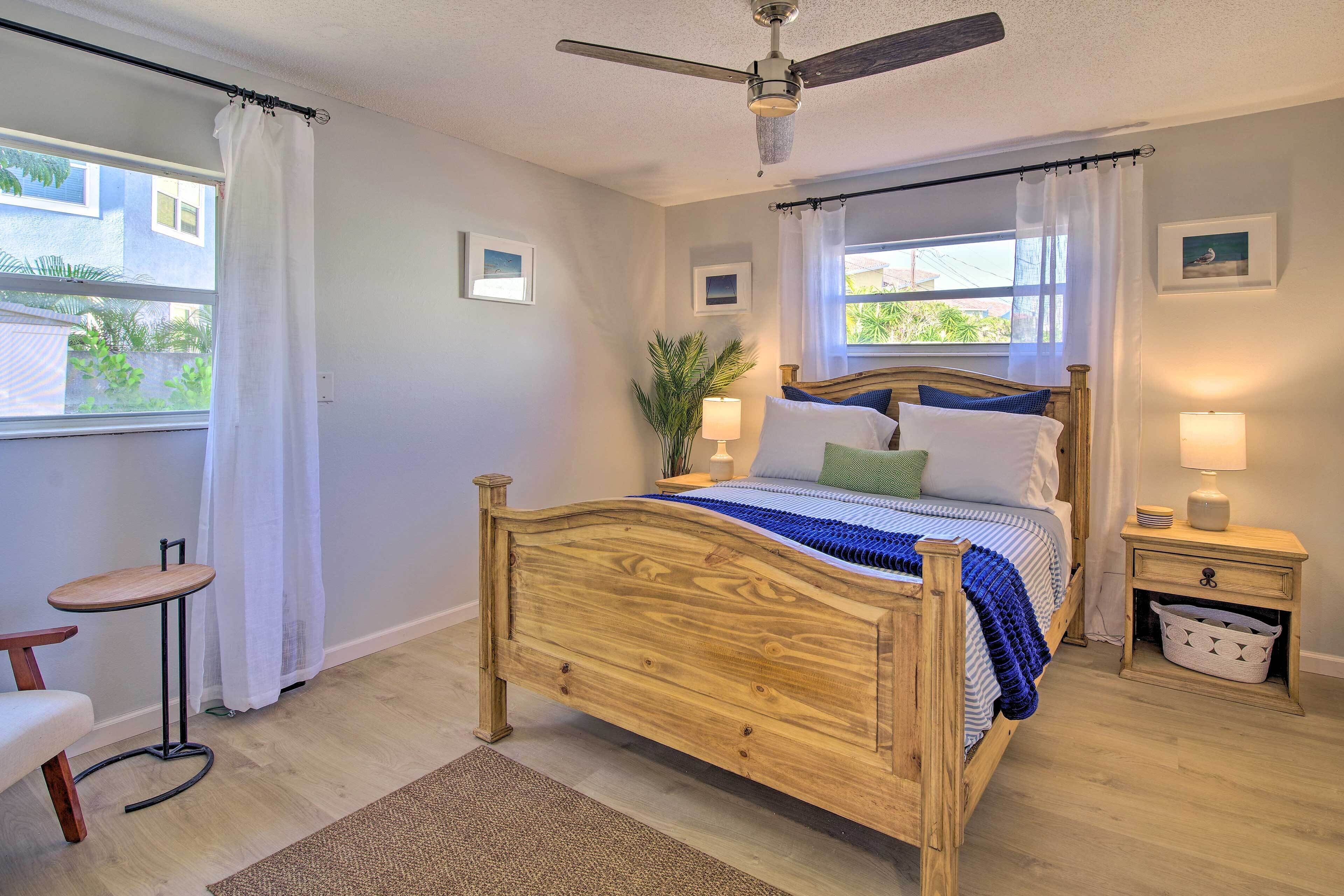 Quarto com cama de madeira, mesa de cabeceira com abajur, uma pequena mesa e uma cadeira.