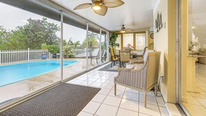 Um pátio amplo com piscina, ventilador de teto e área de refeições com cadeiras e mesa.