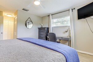 Quarto com cama, escrivaninha, cadeira, cômoda, televisão e janela.