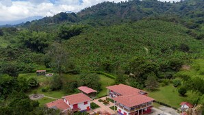 Uma casa grande com piscina, rodeada por vegetação exuberante e colinas ao fundo.