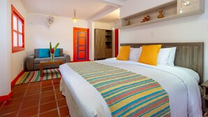 Quarto de hotel com uma cama grande, um sofá, um armário de madeira e uma porta vermelha.