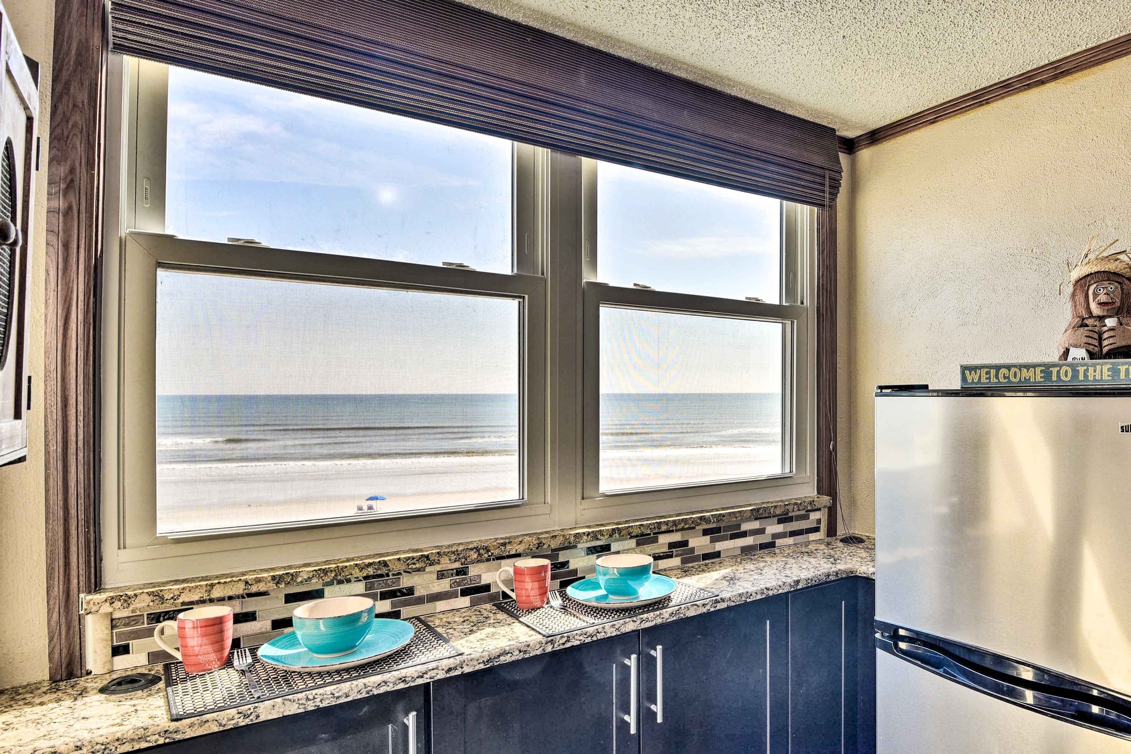 Cozinha com vista para o oceano através de uma janela grande, geladeira de aço inoxidável e um letreiro de boas-vindas.