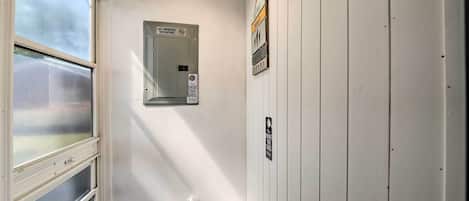 Um corredor estreito com uma janela à esquerda, uma porta com placa de 'Proibido Fumar' e um interruptor de luz fixado na parede.