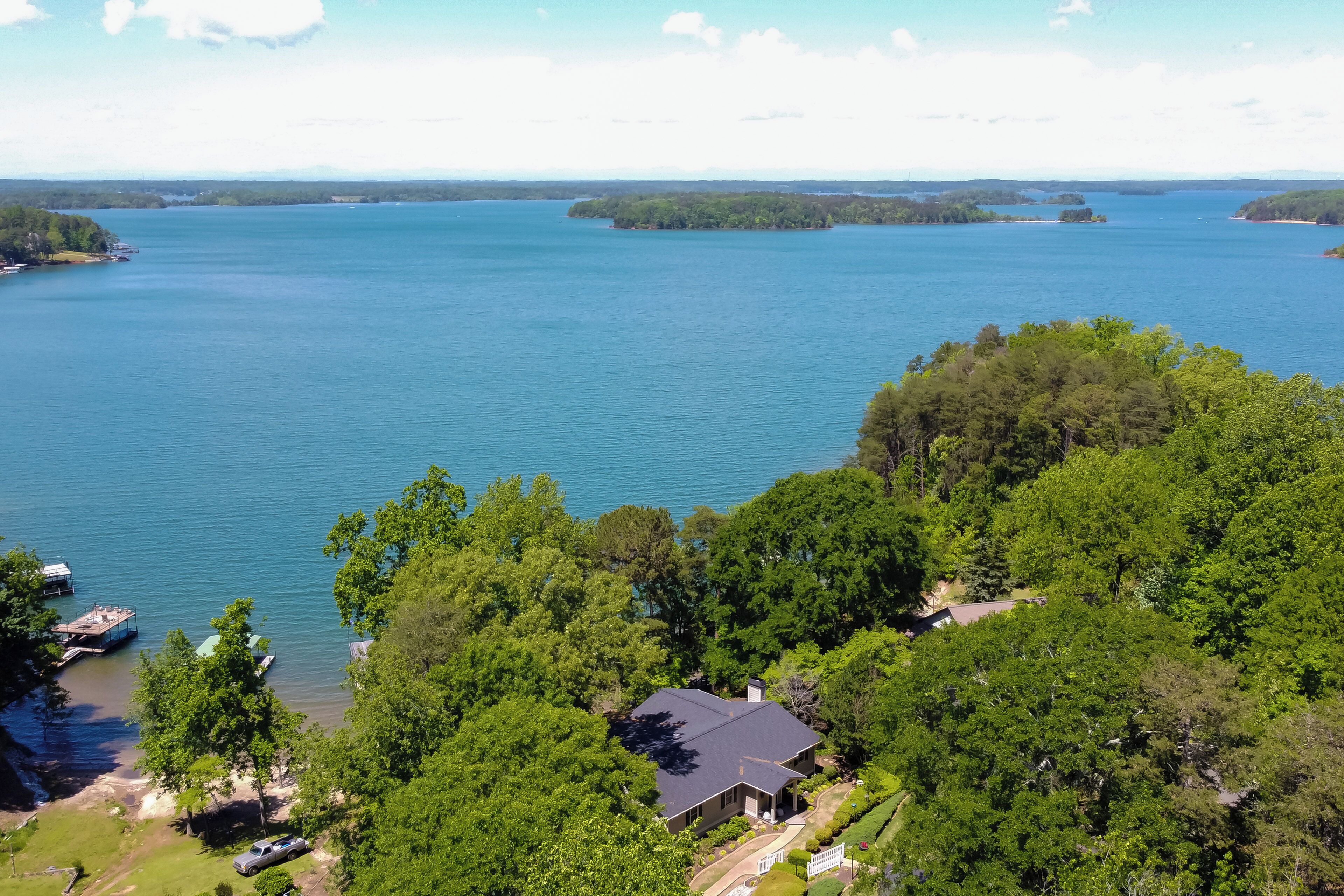 Uma casa cercada por floresta densa, com vista para uma grande extensão de água e barcos atracados perto.