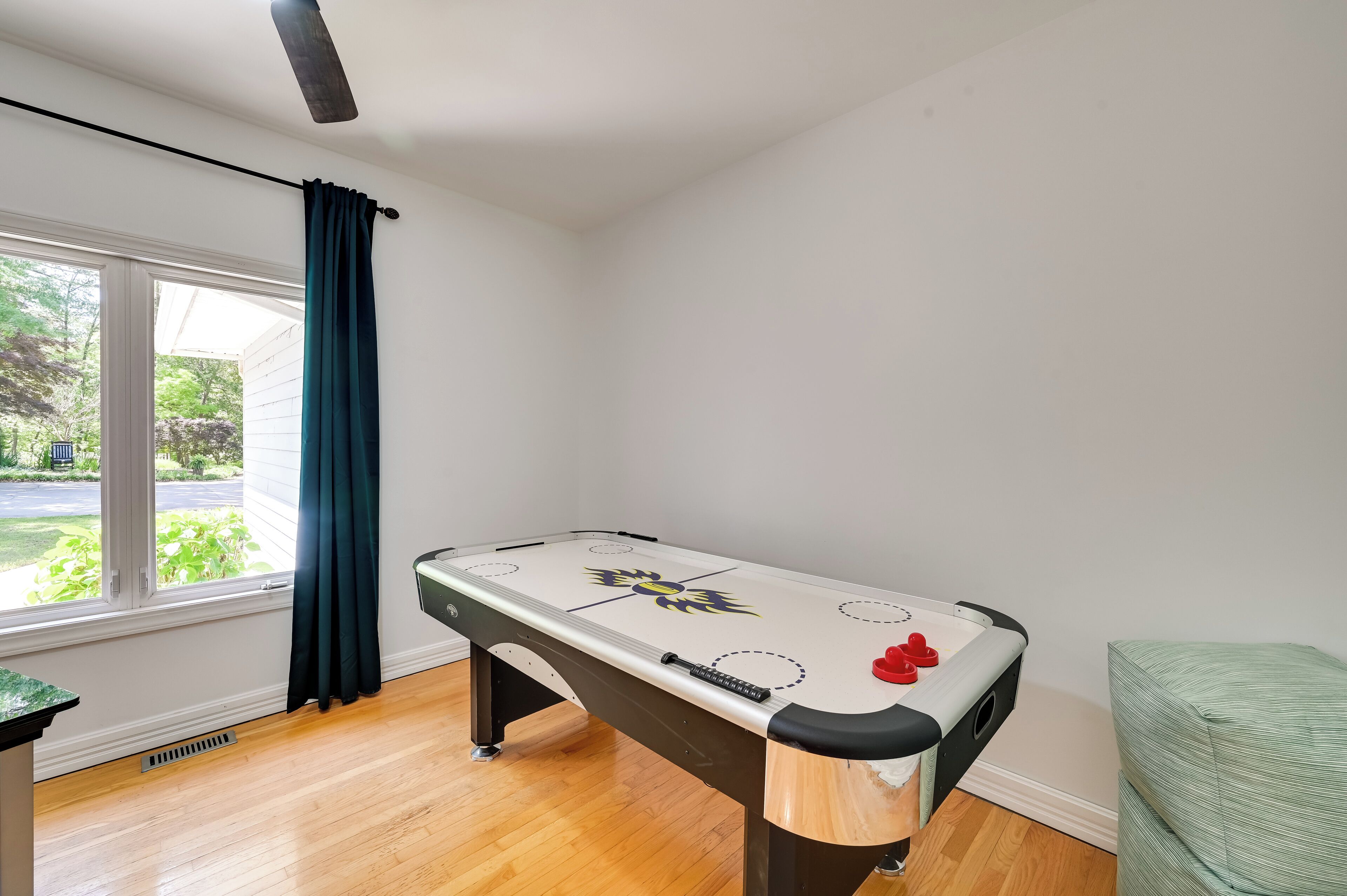 Quarto com mesa de bilhar, janela com cortinas e um banco estofado verde.