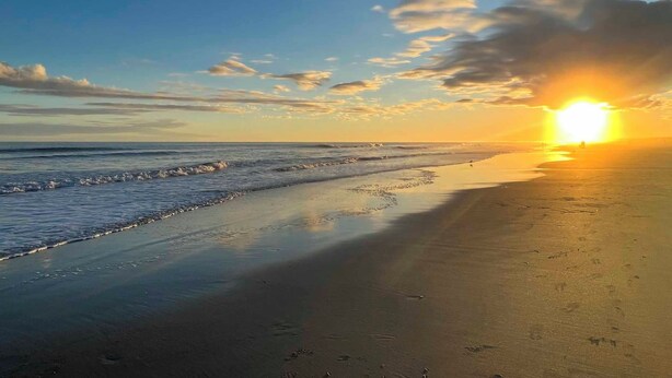 Uma praia com um pôr do sol, ondas e pegadas.