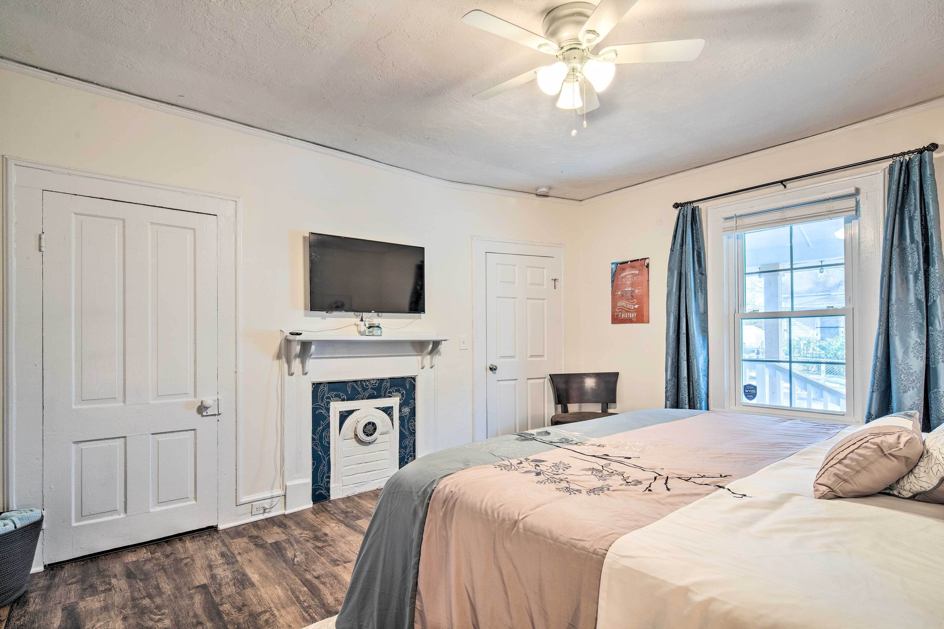 Quarto com cama, televisão sobre a lareira, janela com cortinas e ventilador de teto.