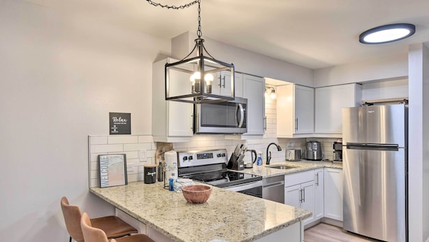 Cozinha moderna com ilha central, eletrodomésticos de aço inoxidável e luminária pendente.