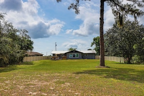 Um imóvel residencial com um quintal cercado, uma casa com telhado de metal e um céu claro.