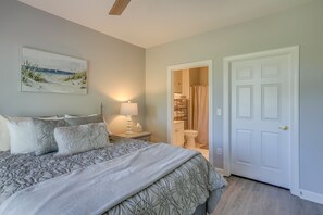 Quarto com cama, mesa de cabeceira, abajur e porta para um banheiro.