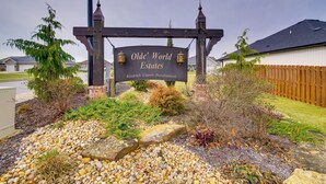 Placa para Olde' World Estates, com entrada ajardinada, pedras, arbustos e cerca de madeira.