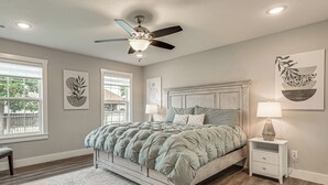 Quarto com cama, mesa de cabeceira, abajur, ventoinha no teto e obras de arte nas paredes.