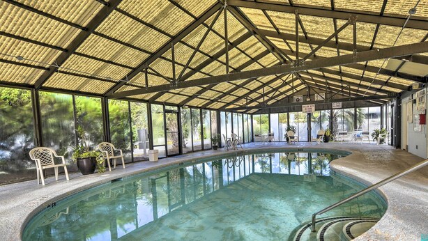 Piscina interior com cobertura, água cristalina e algumas cadeiras e plantas em vasos ao redor da borda.