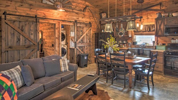 Interior rústico de cabana com sofá, mesa de jantar, cadeiras e área de cozinha.