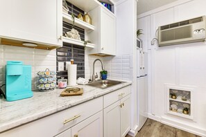 Cozinha com armários brancos, bancada de mármore, pia, cafeteira e objetos decorativos.