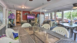 Uma área de refeições com mesa de vidro, cadeiras de plástico branco e um ventilador de teto.