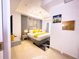 Quarto de hotel moderno com uma cama grande, uma mesa de cabeceira, uma luminária, um quadro na parede e vista para um edifício.