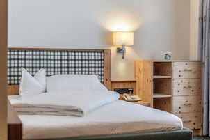 Quarto de hotel com cama, mesa de cabeceira com abajur, telefone e armário de madeira com gavetas.