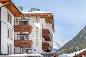 Um hotel com várias varandas, um telhado coberto de neve e montanhas ao fundo.