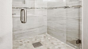 Um chuveiro moderno com porta de vidro, ducha de chuva e barras de apoio.